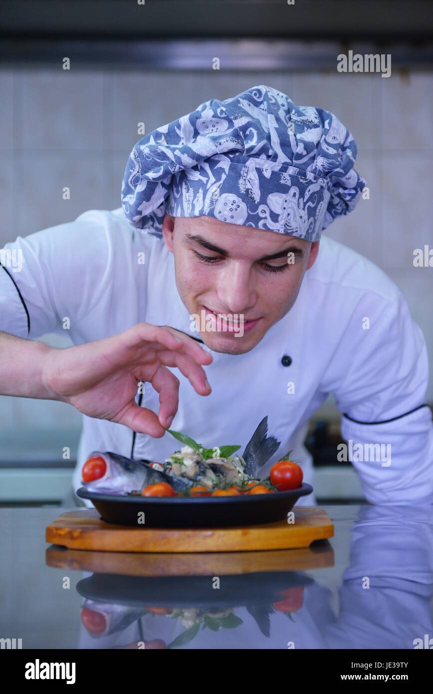 Handsome chef dressed in white uniform decorating pasta salad and ...