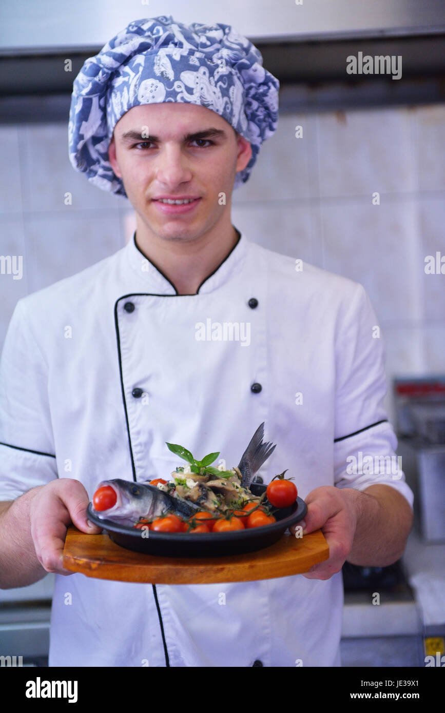 Handsome chef dressed in white uniform decorating pasta salad and ...