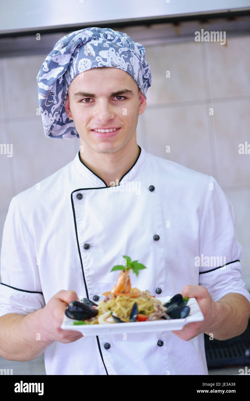 Handsome chef dressed in white uniform decorating pasta salad and ...