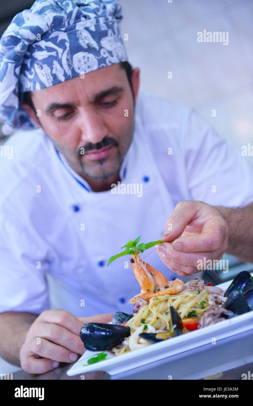 Handsome chef dressed in white uniform decorating pasta salad and ...