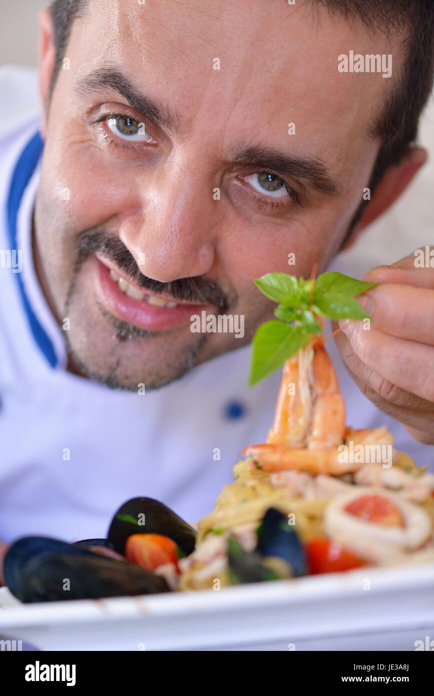 Handsome chef dressed in white uniform decorating pasta salad and ...