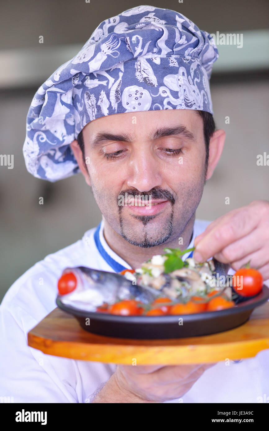 Handsome chef dressed in white uniform decorating pasta salad and ...