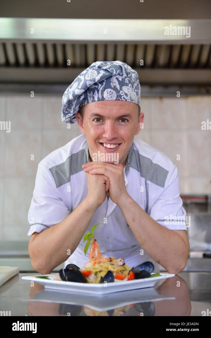 Handsome chef dressed in white uniform decorating pasta salad and ...