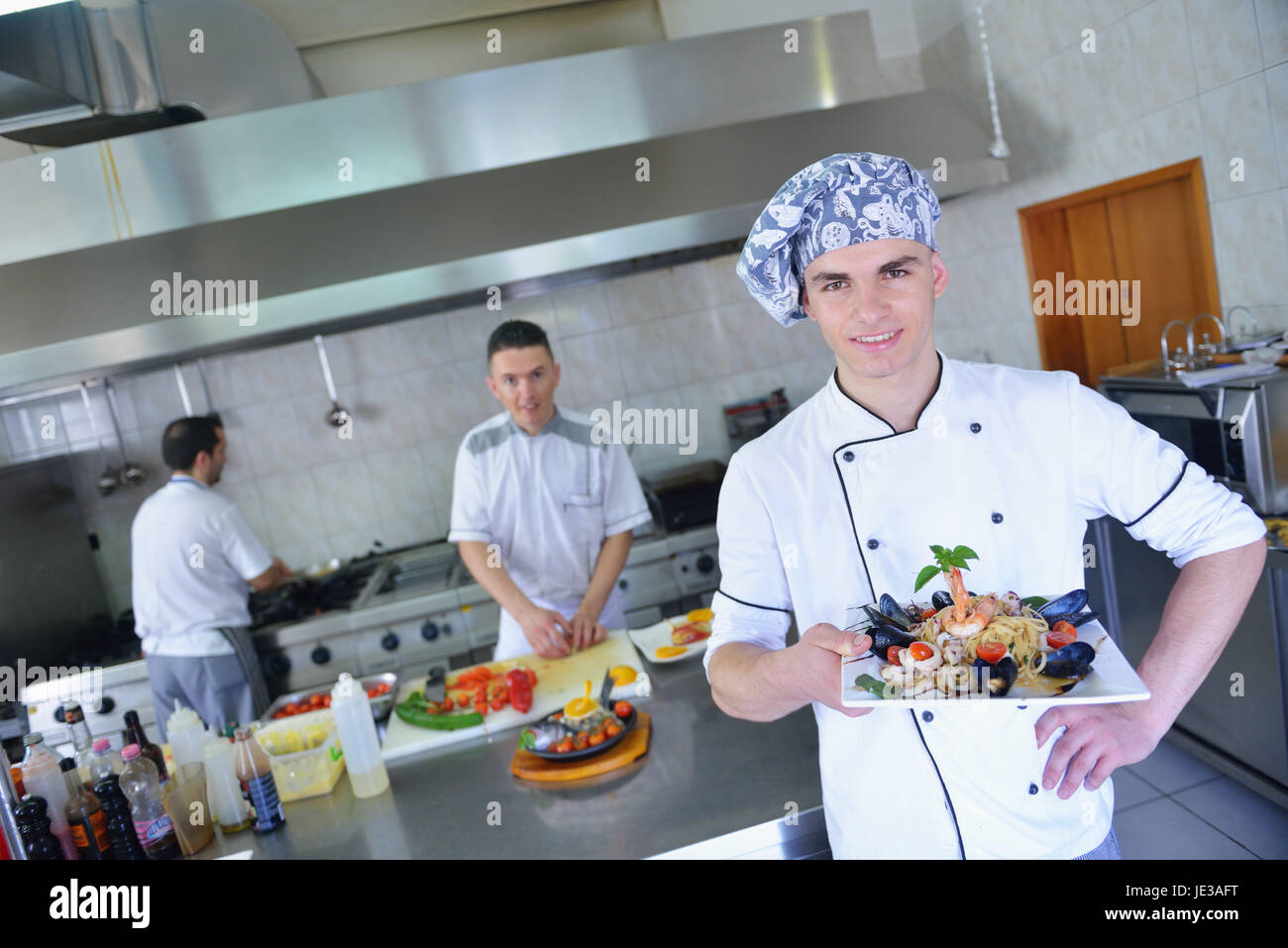 Handsome chef dressed in white uniform decorating pasta salad and ...