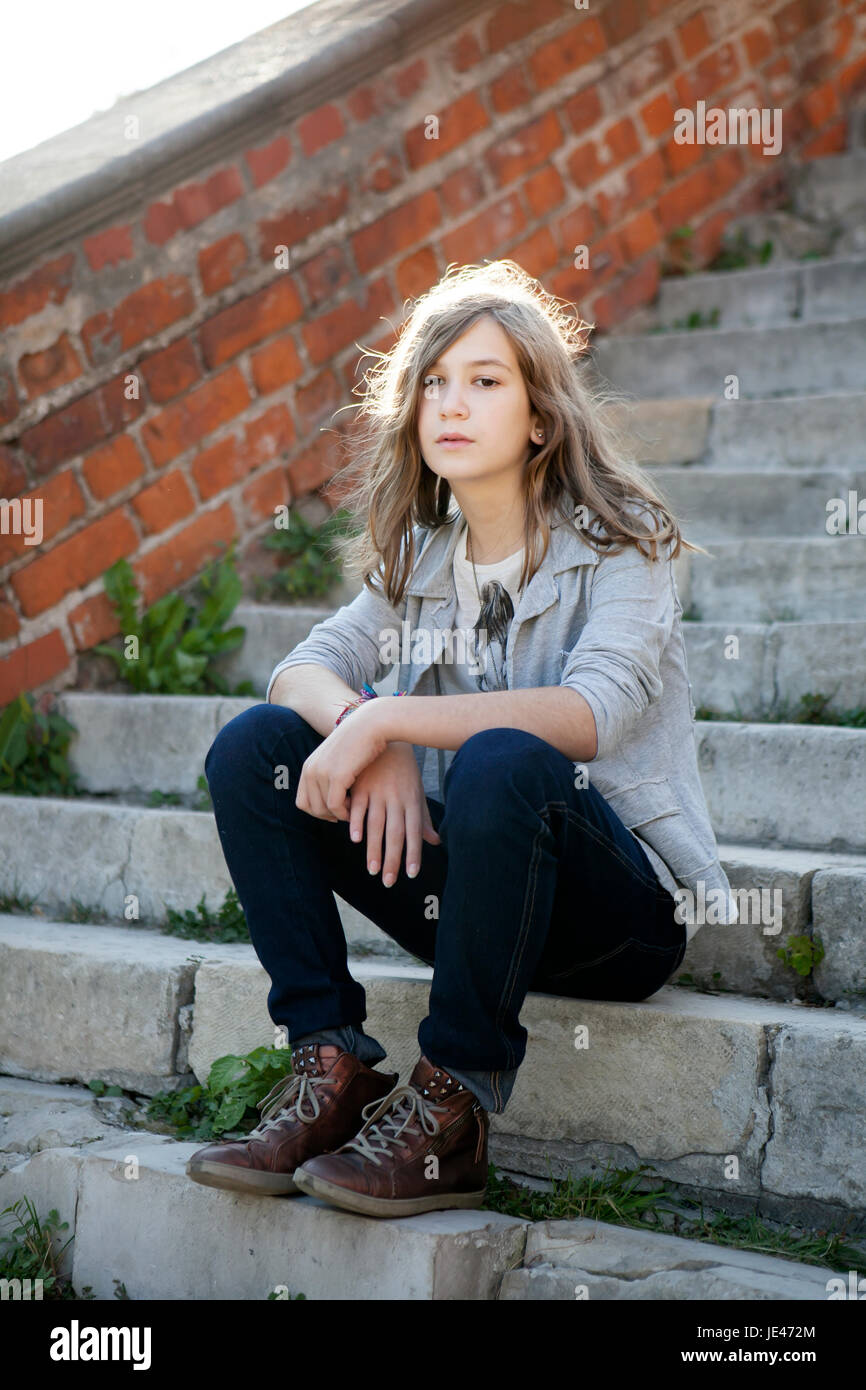 A sad girl with long hair in jeans of thirteen sits on the steps Stock ...