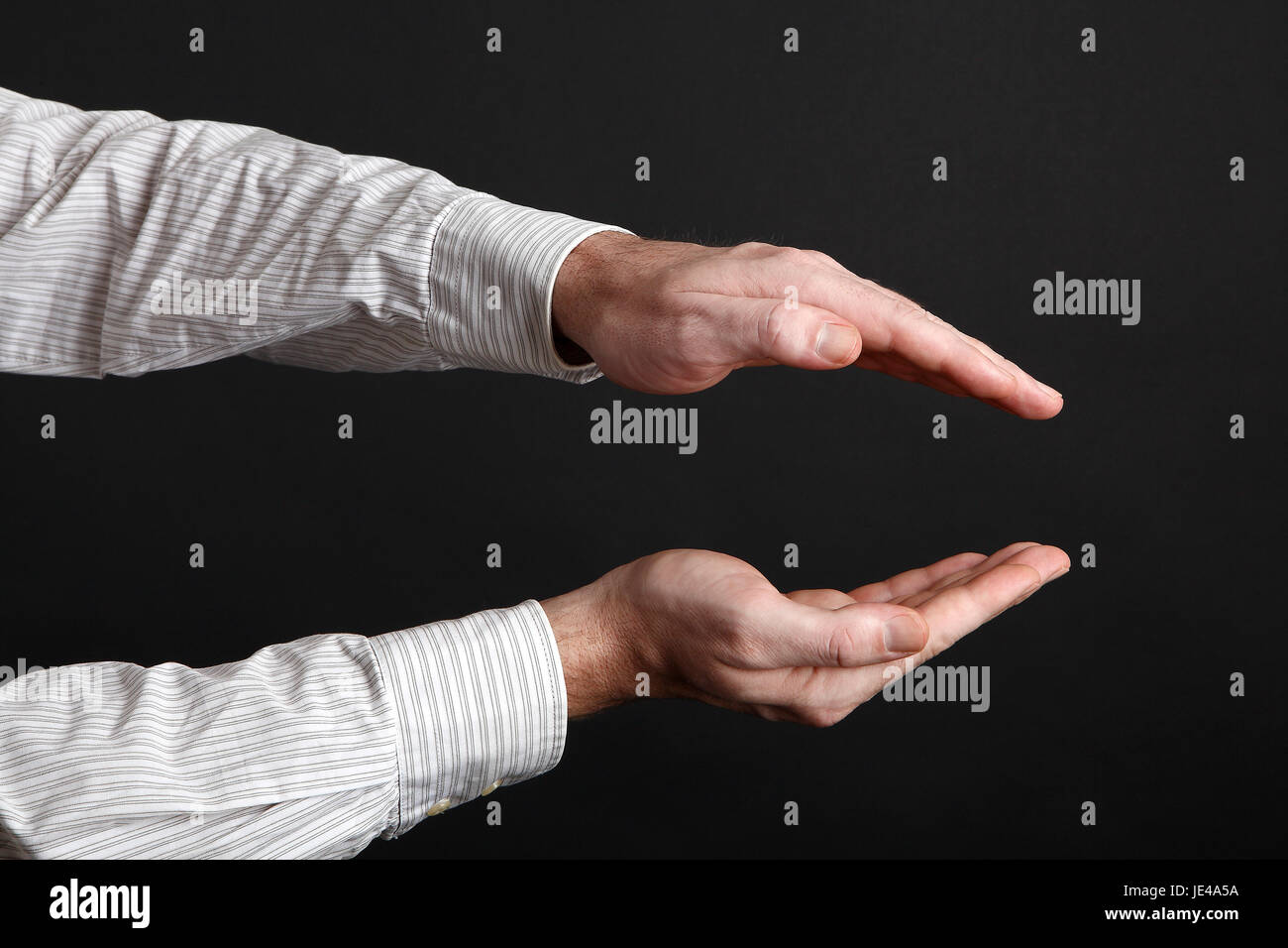 Caucasian male hands protect something in front of a black background ...