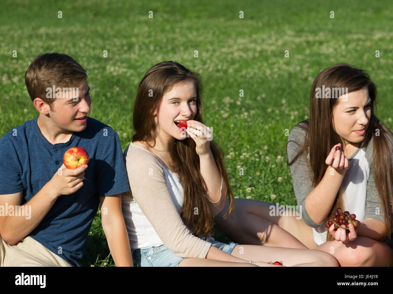 Trio of happy Caucasian teenagers eating fruit outdoors Stock Photo - Alamy