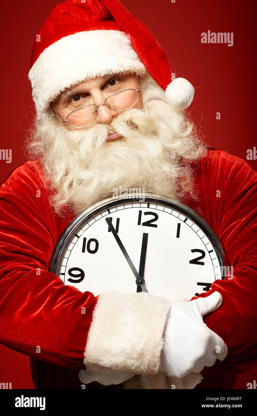 Senior man in costume of Santa holding clock showing five minutes to ...