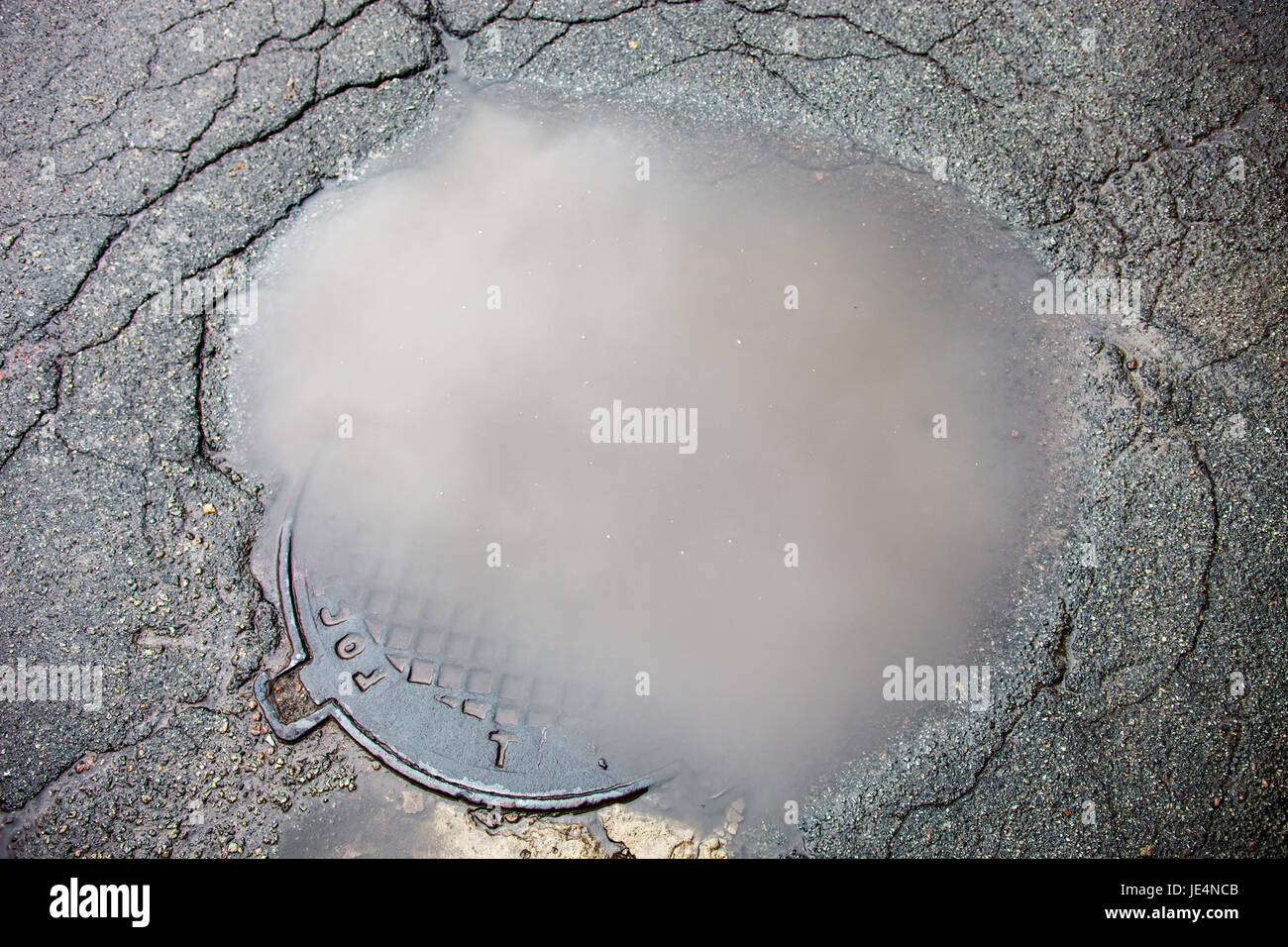 The puddle on the metal manhole in asphalt surface Stock Photo - Alamy