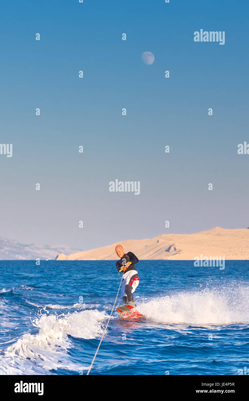Wakeboarder in wetsuit riding in sunset. Wakeboarding is a surface ...