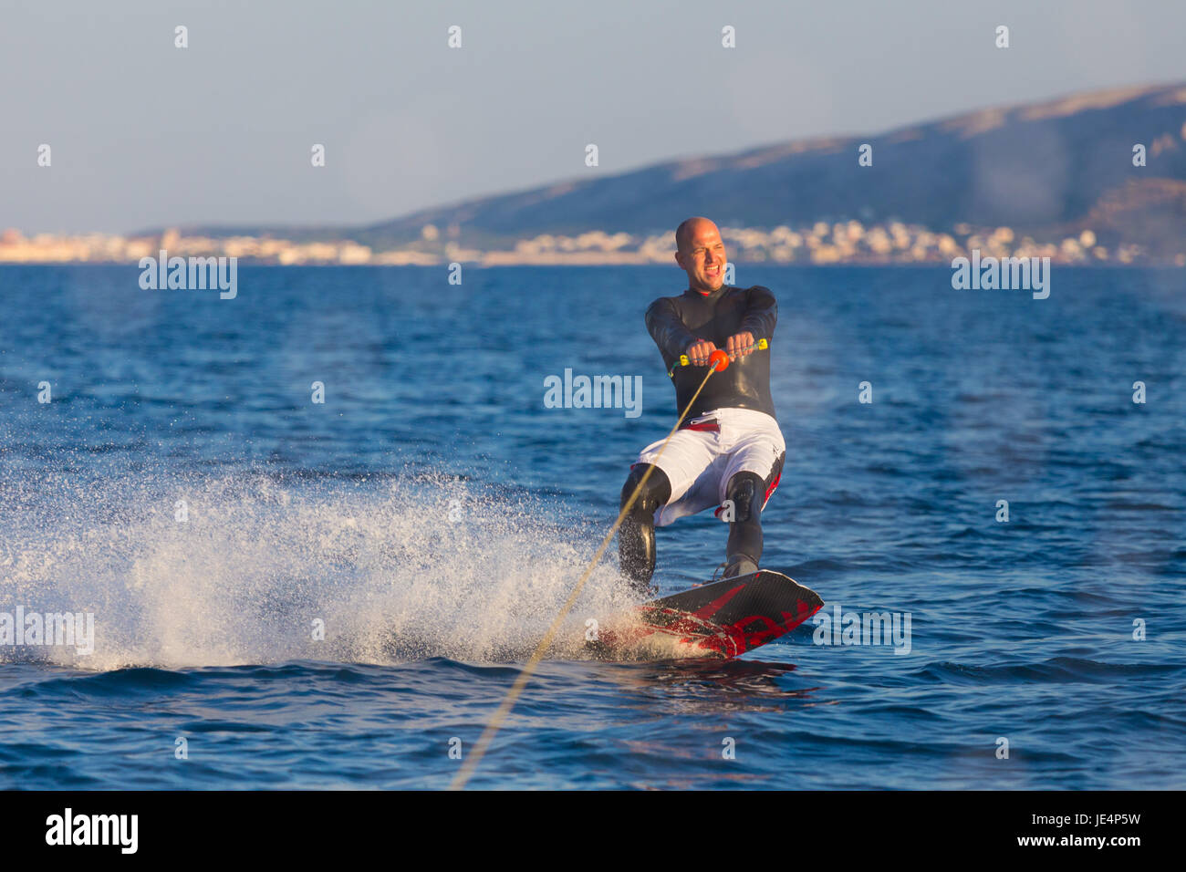 Wakeboarder in wetsuit riding in sunset. Wakeboarding is a surface ...