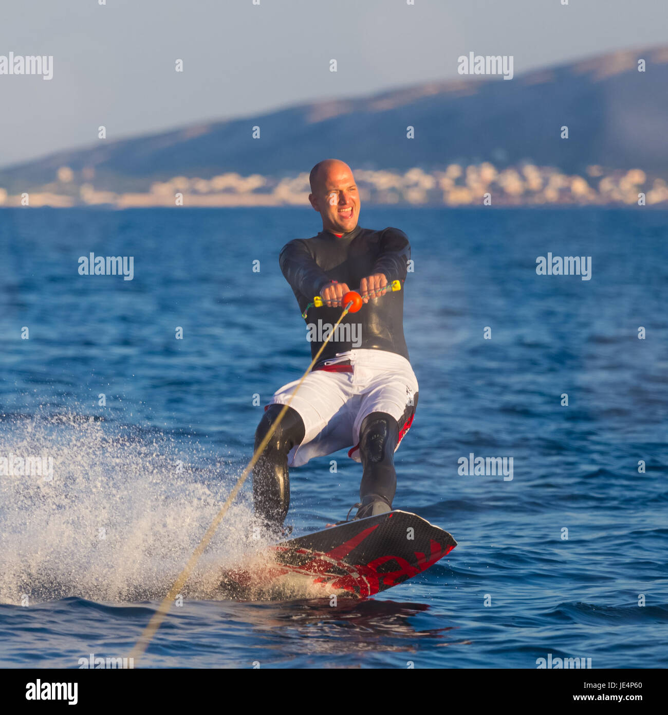 Wakeboarder in wetsuit riding in sunset. Wakeboarding is a surface ...