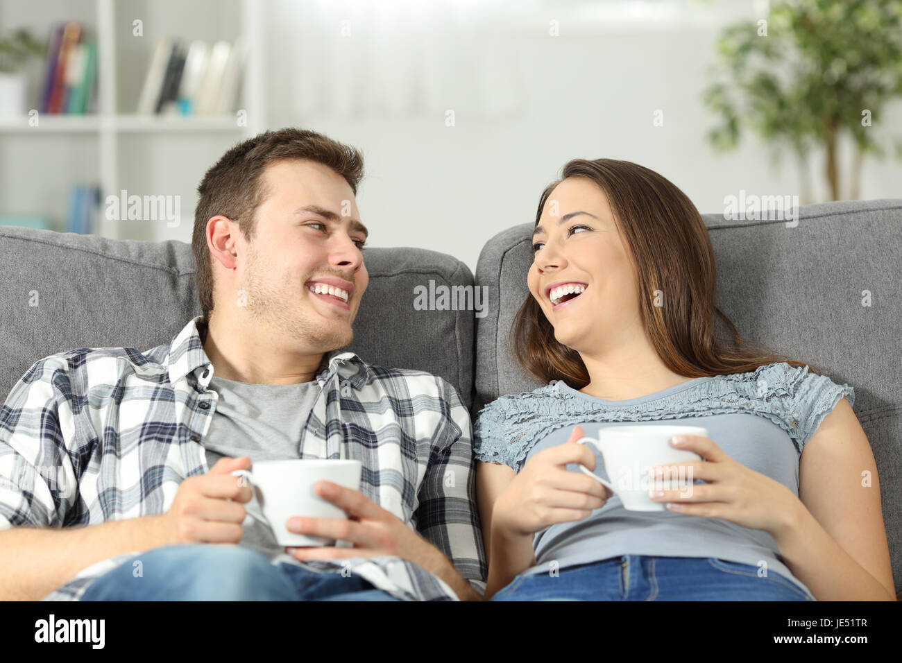 Relaxed couple talking and holding coffee cups sitting on a sofa in the ...