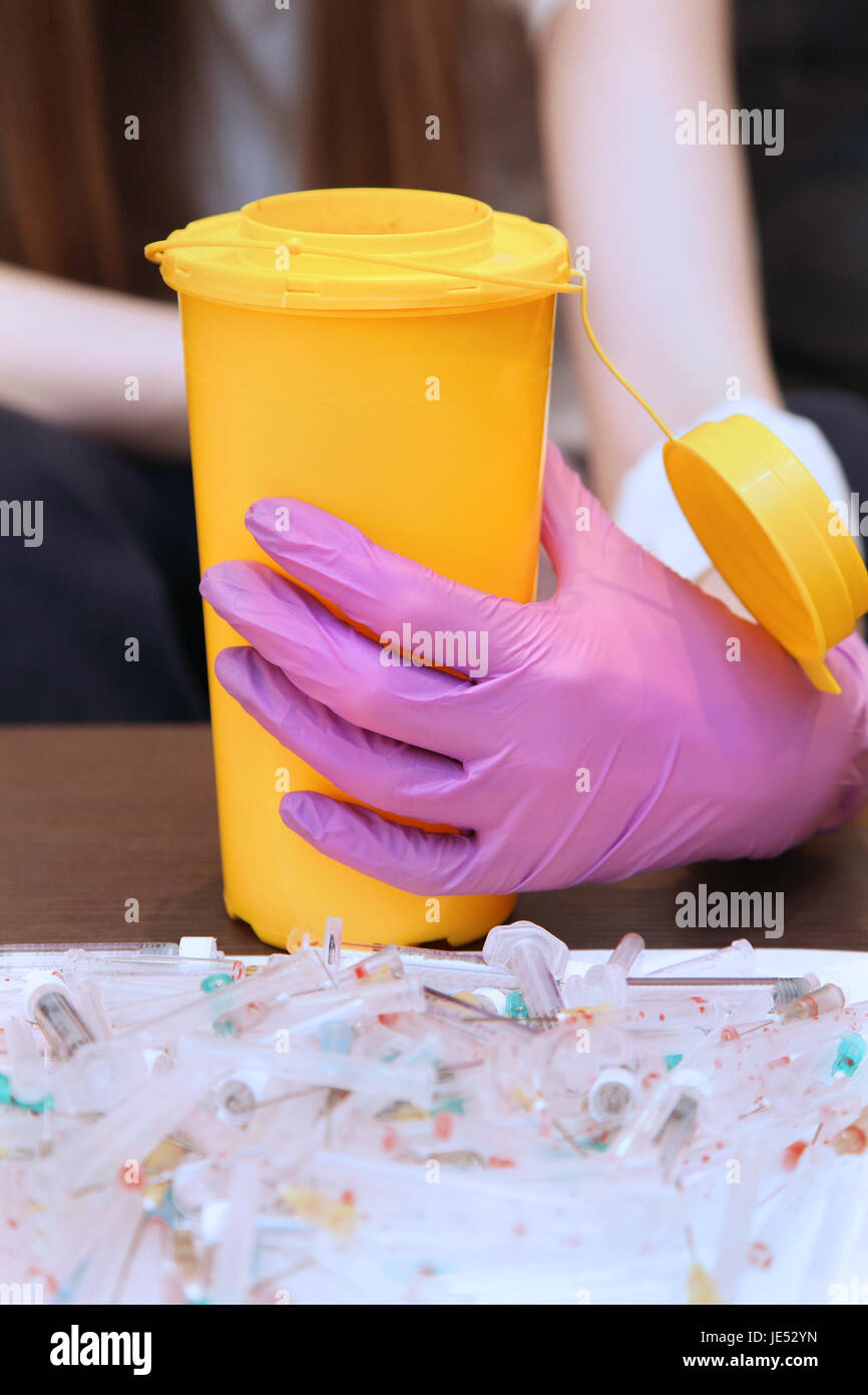 Female hand holding yellow waste container with used syringes and ...