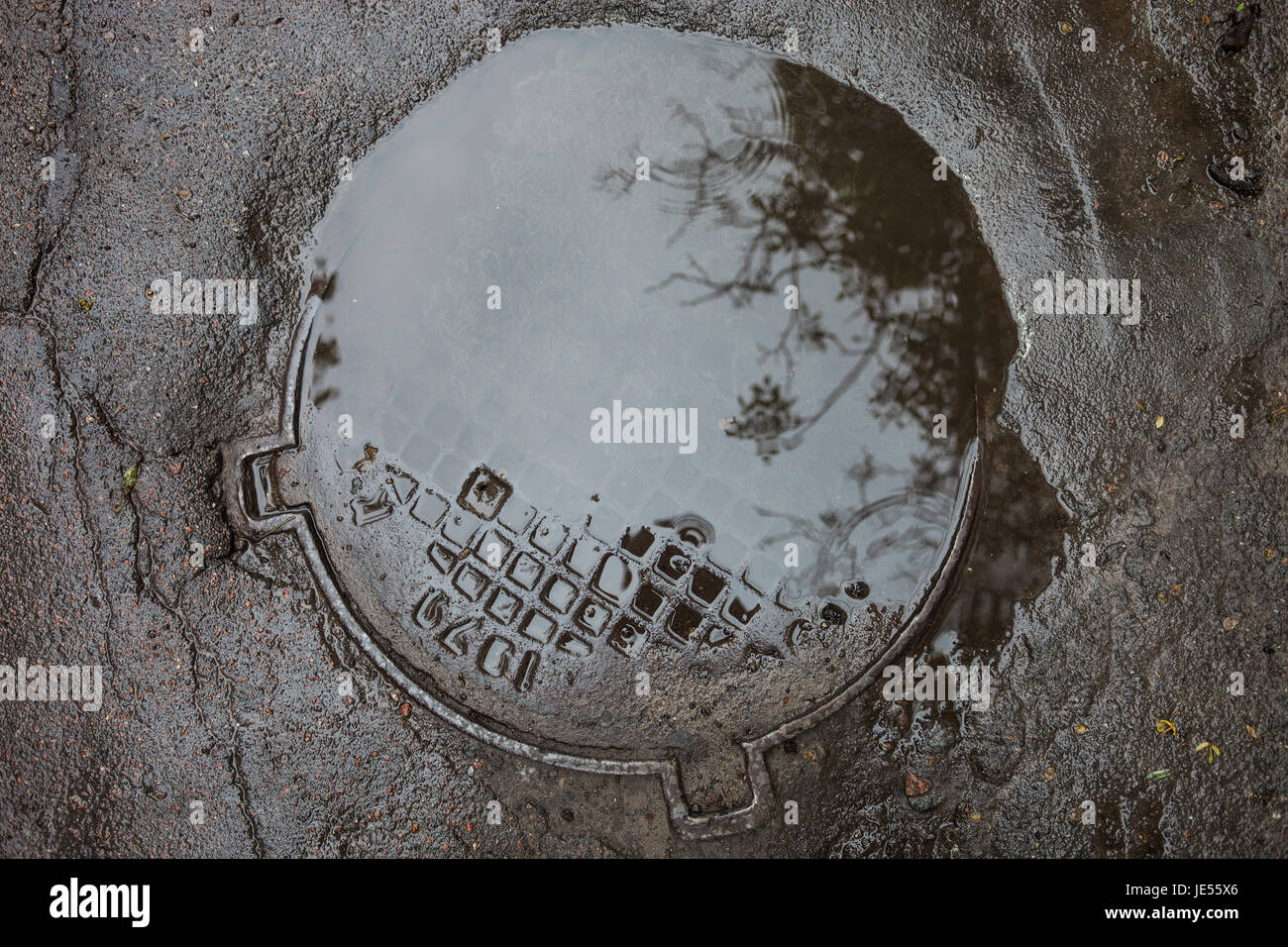 The puddle on the metal manhole in asphalt surface Stock Photo - Alamy