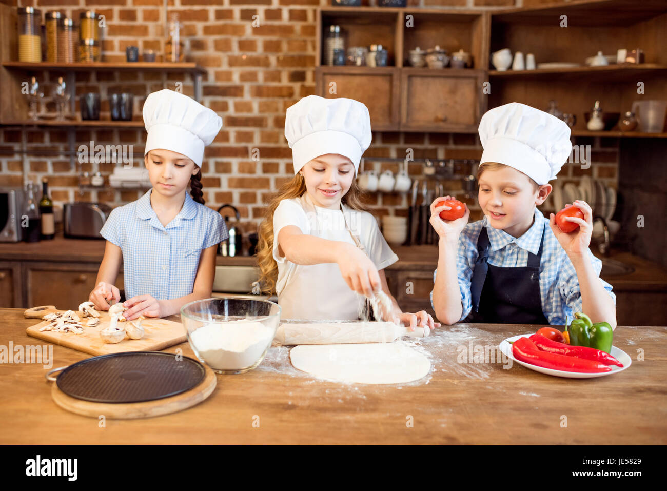 children making pizza dough and preparing pizza ingredients in kitchen ...