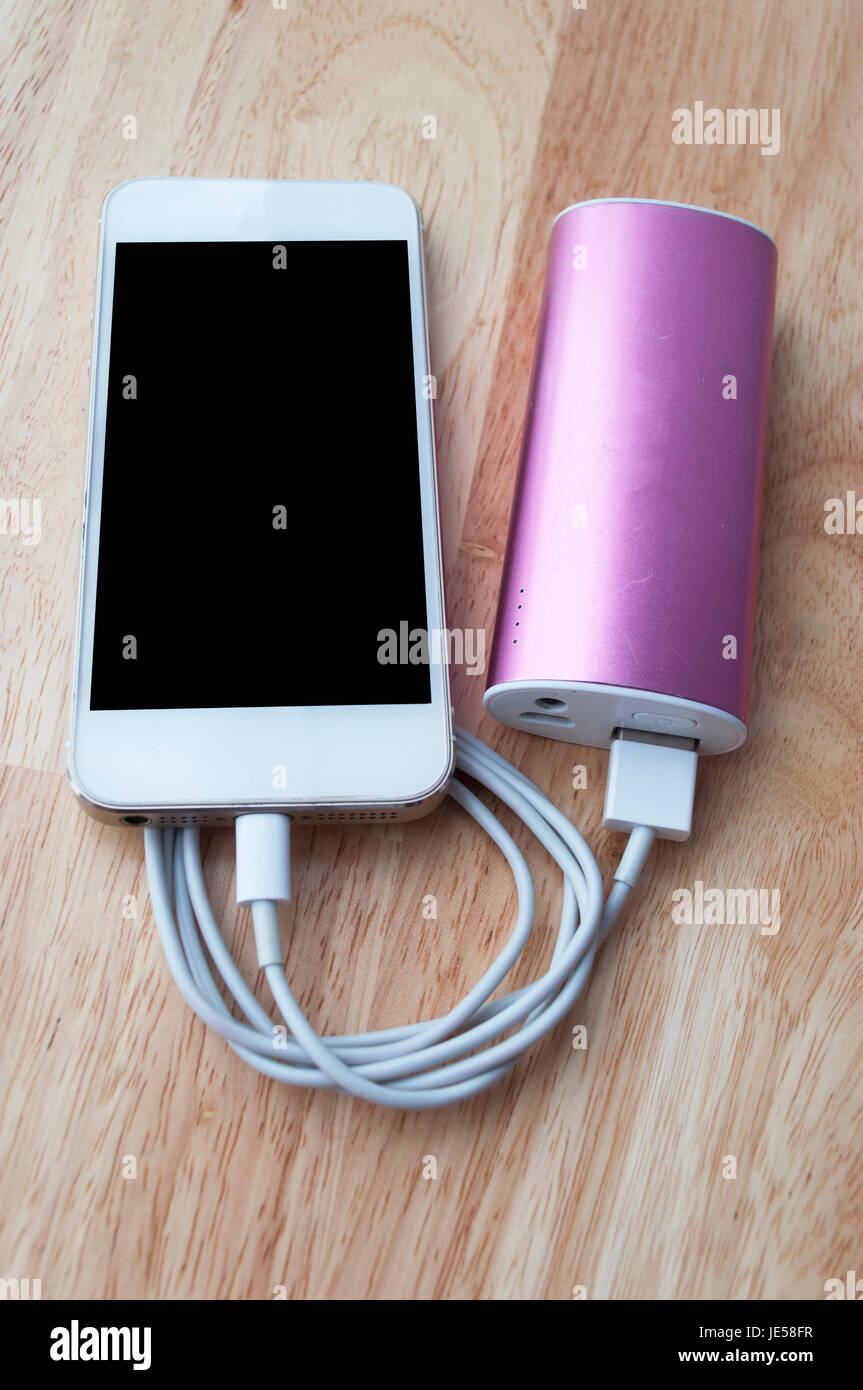 Smartphone charging with pink power bank on wood background, selective ...