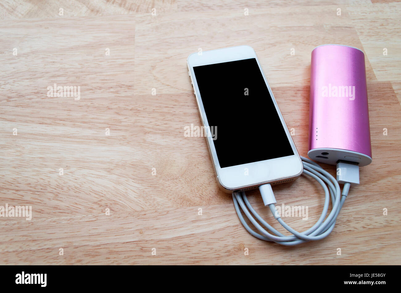 Smartphone charging with pink power bank on wood background, selective ...