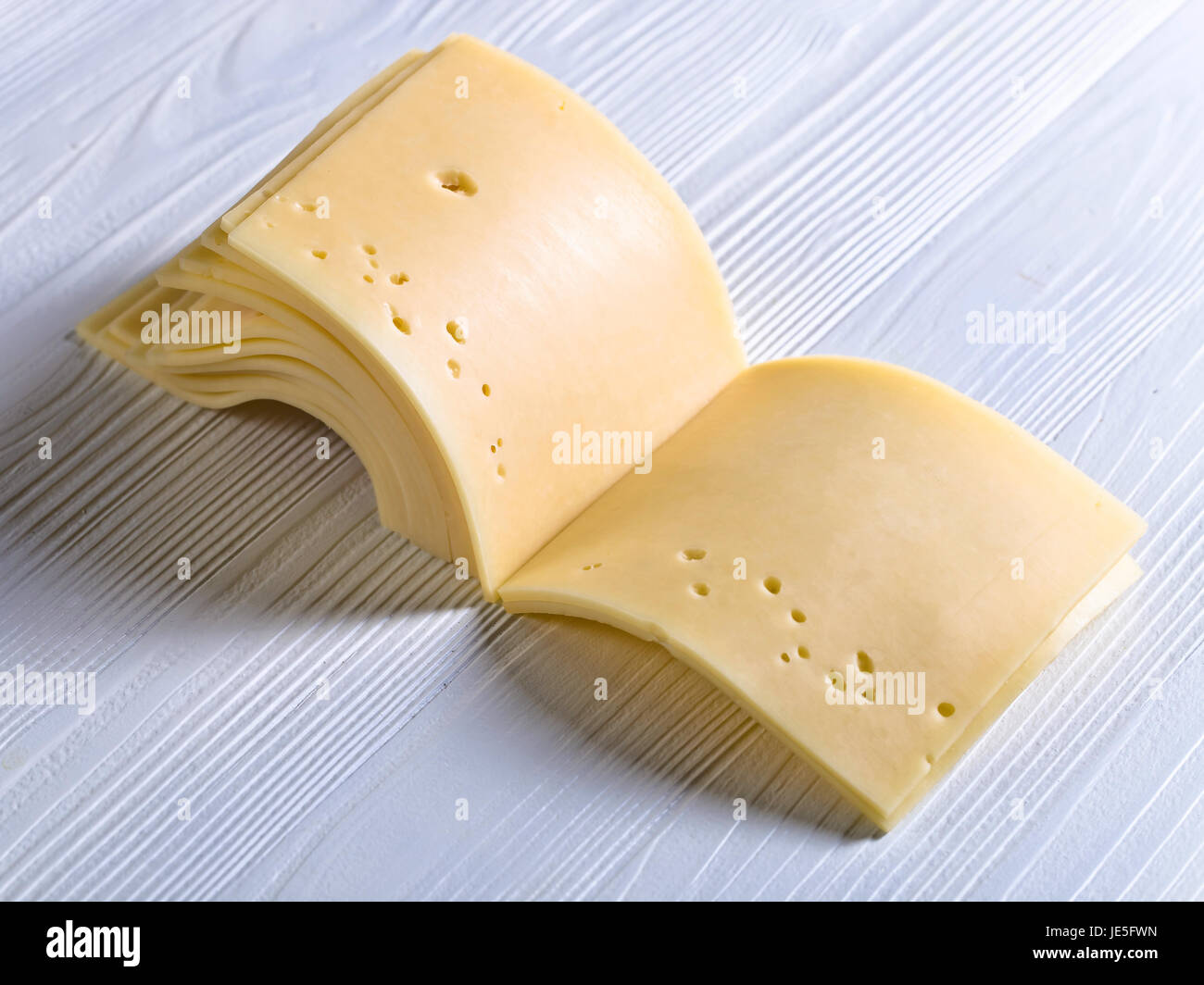 Slices of cheese folded like a book on a white wooden table Stock Photo ...