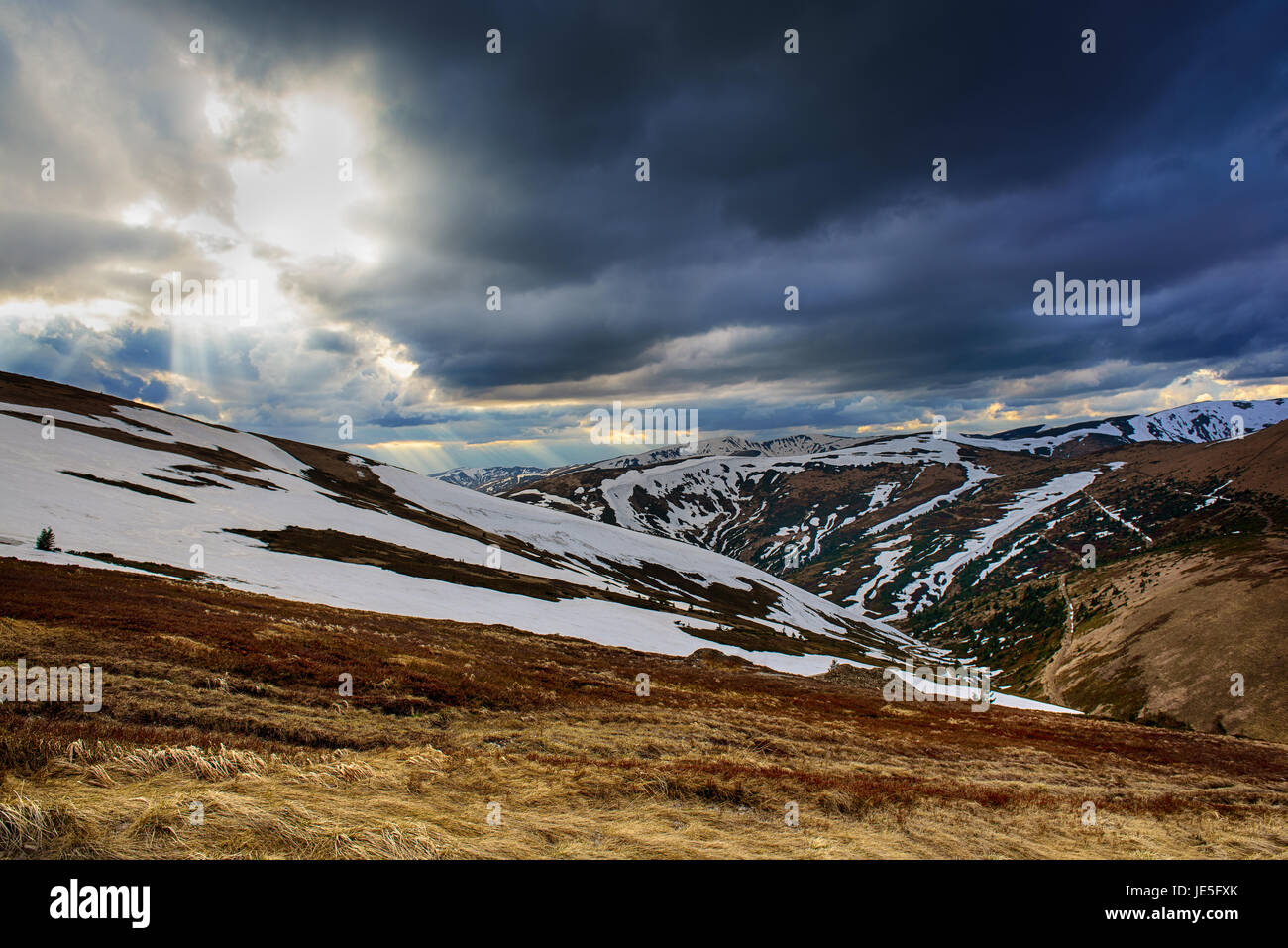 Spring mountain landscape with snow and grass. Dramatic clouds lying on ...