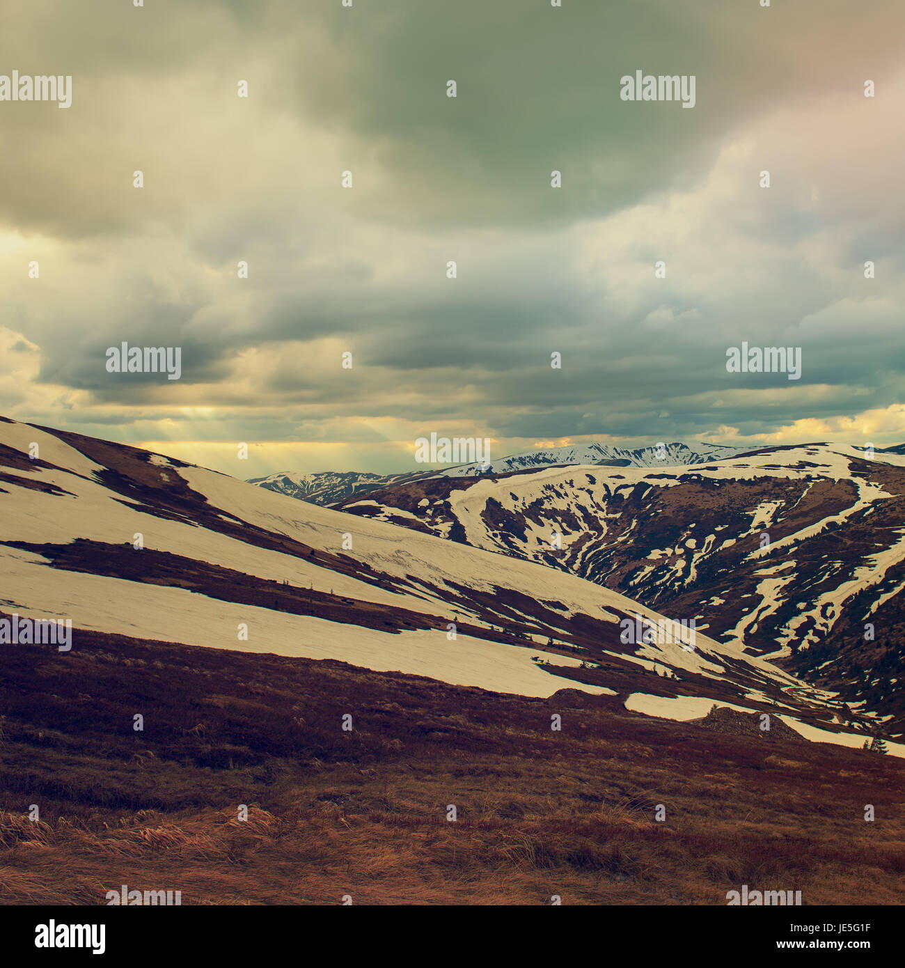 Spring mountain landscape with snow and grass. Dramatic clouds lying on ...