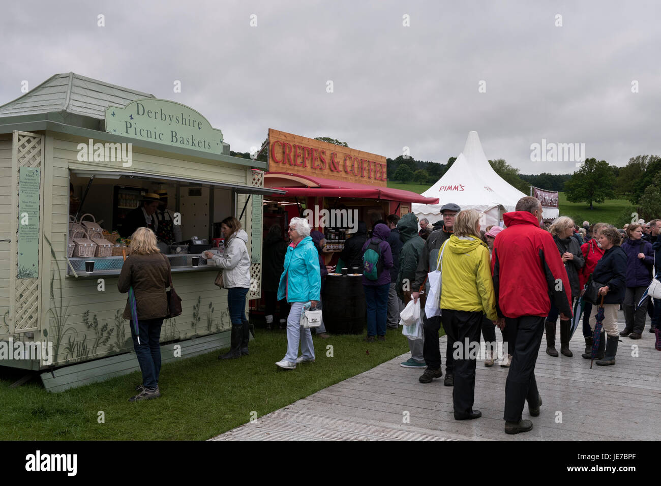 Crowd of people walking by food & drink stalls, some stop for ...