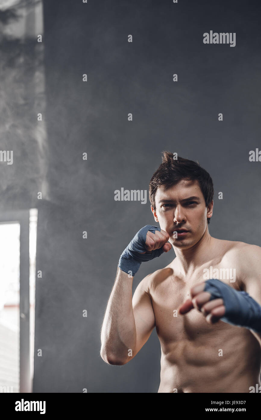 Strong boxer in the rays of the sun and smoke training hands with ...