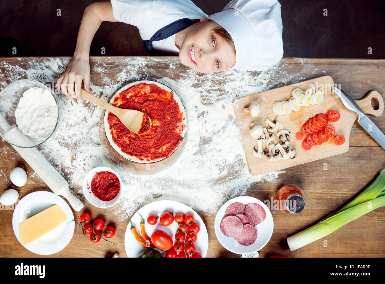 top view of boy making pizza with pizza ingredients, tomatoes, salami ...