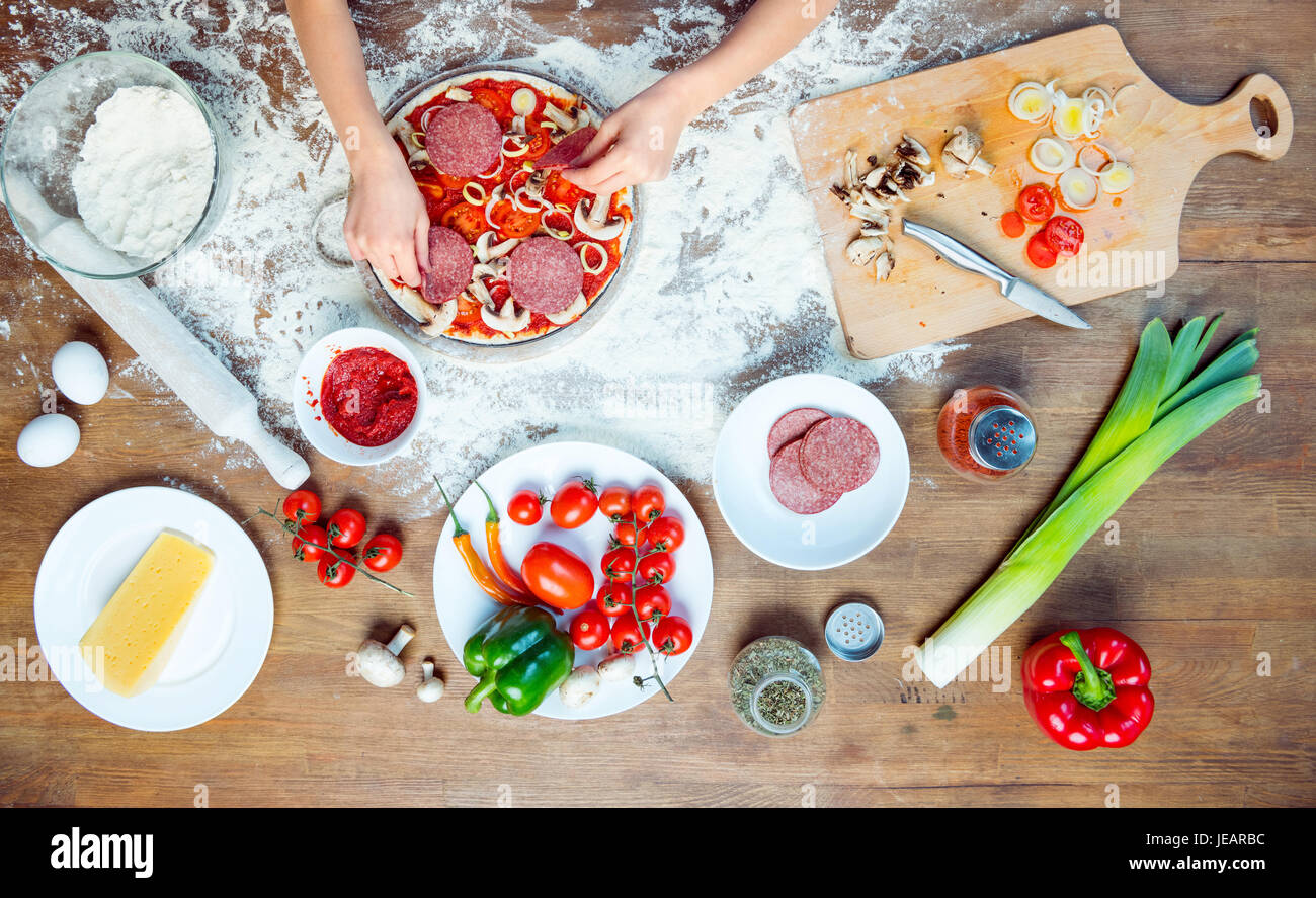 top view of child making pizza with pizza ingredients, tomatoes, salami ...