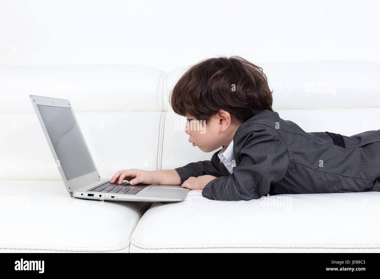 Asian Chinese little boy playing laptop on the couch in the living room ...