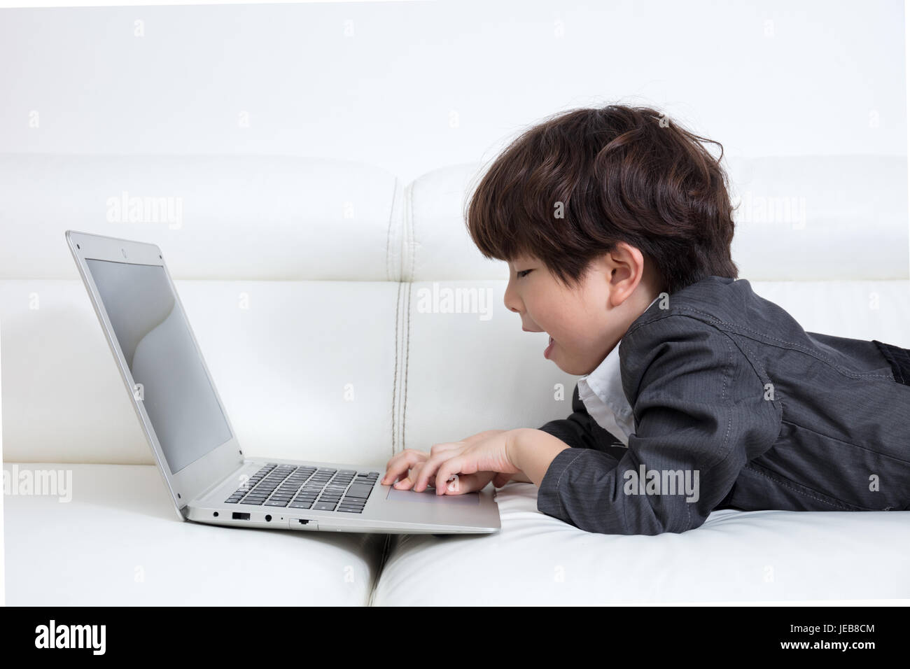 Asian Chinese little boy playing laptop on the couch in the living room ...