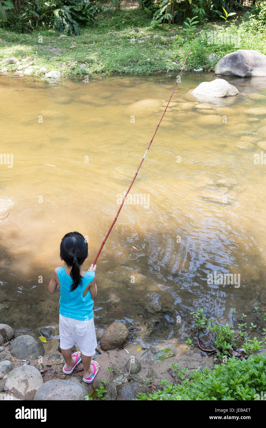 Asian Chinese little girl angling with fishing rod at the river shore ...