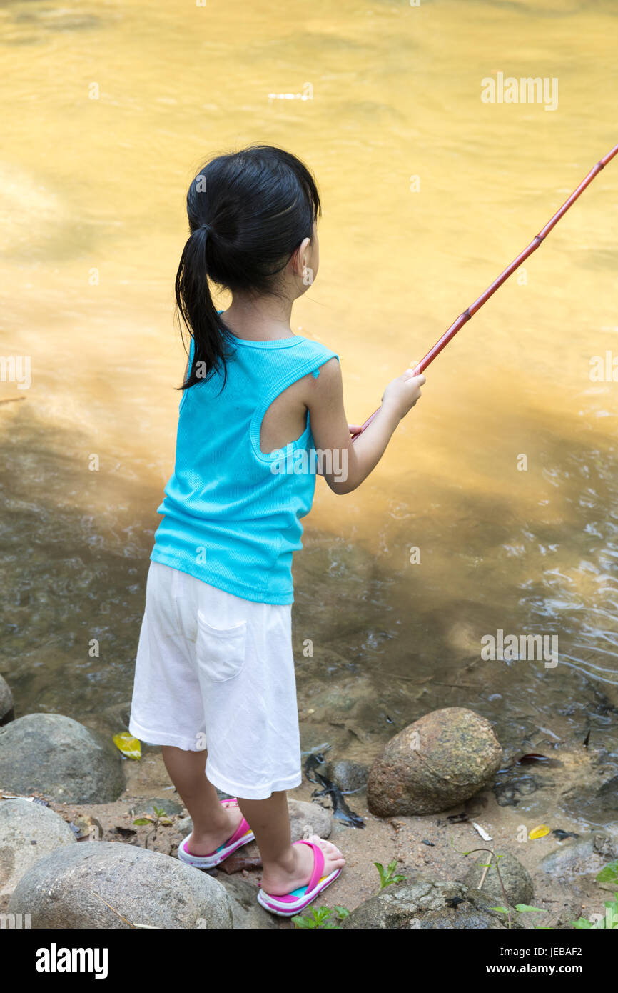 Asian Chinese little girl angling with fishing rod at the river shore ...