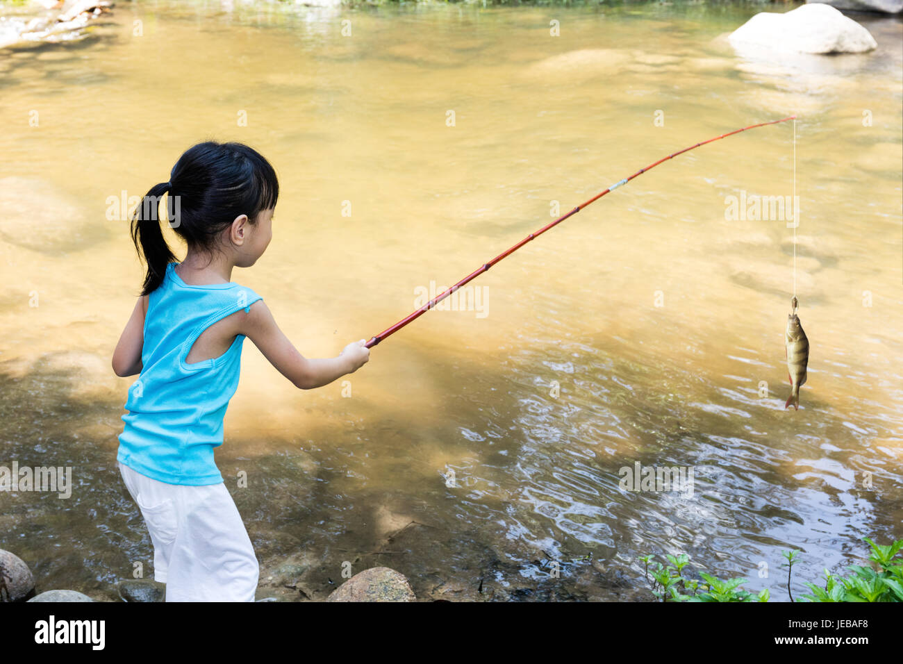 Asian Chinese little girl angling with fishing rod at the river shore ...