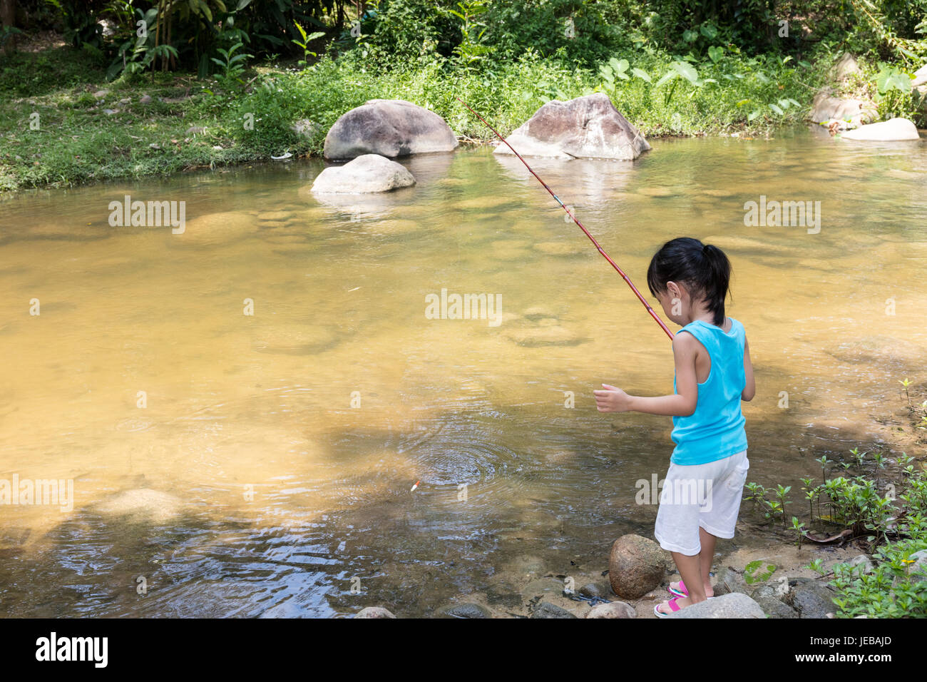 Asian Chinese little girl angling with fishing rod at the river shore ...