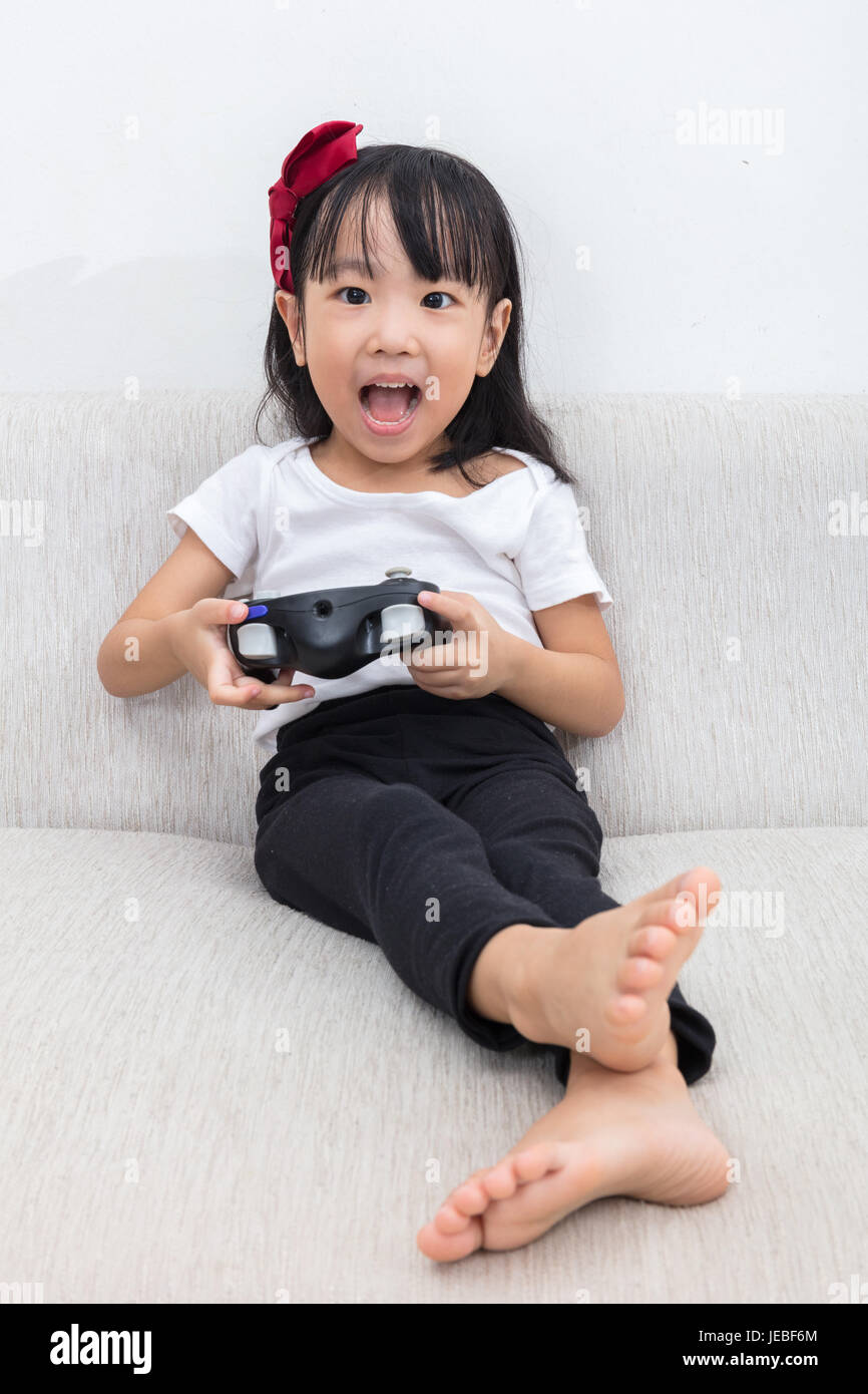 Asian Chinese little girl playing TV games on the sofa in the living ...