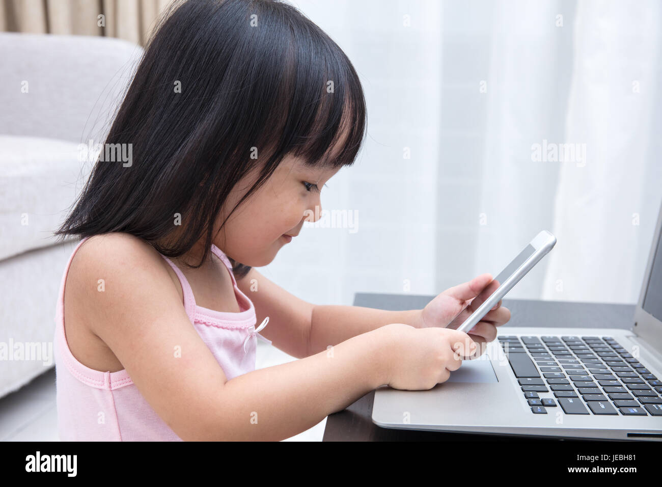 Asian Chinese little girl busy reading mobile phone and laptop in the ...