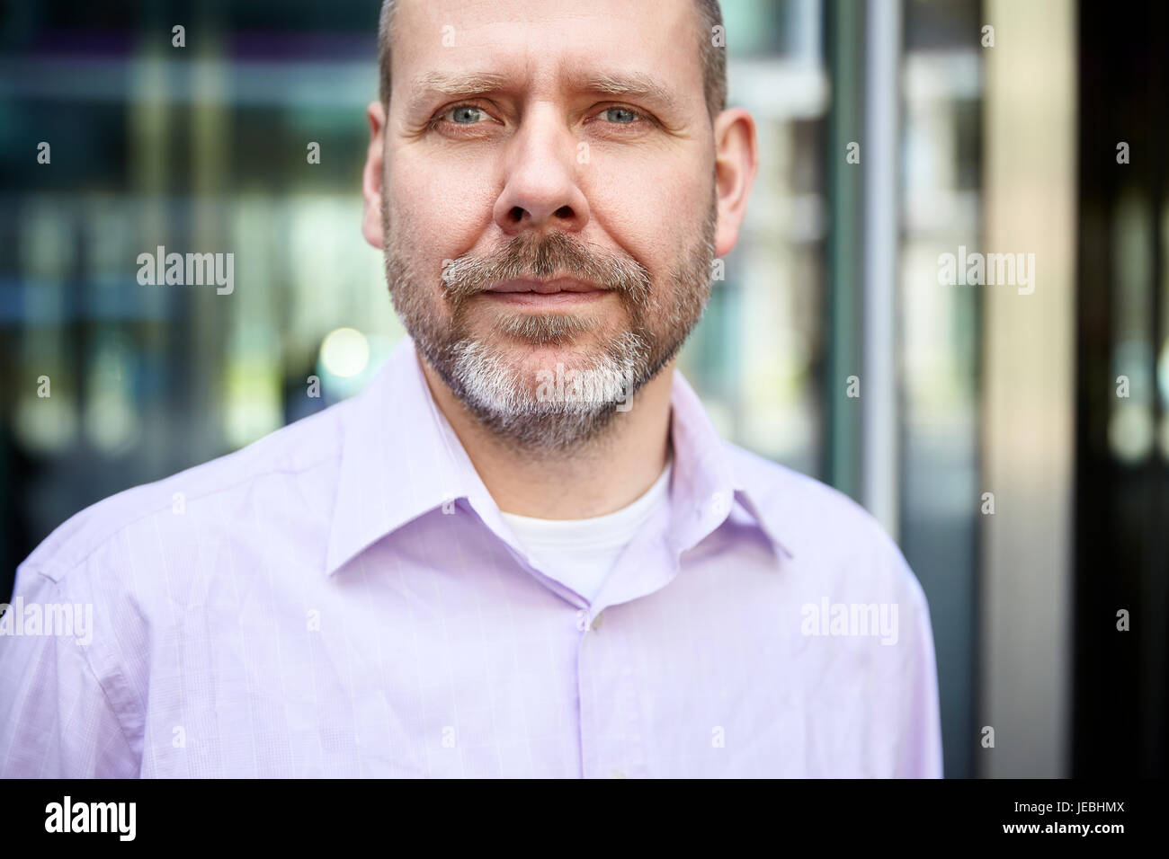 Headshot portrait of middle aged man in pink shirt. He is standing in ...