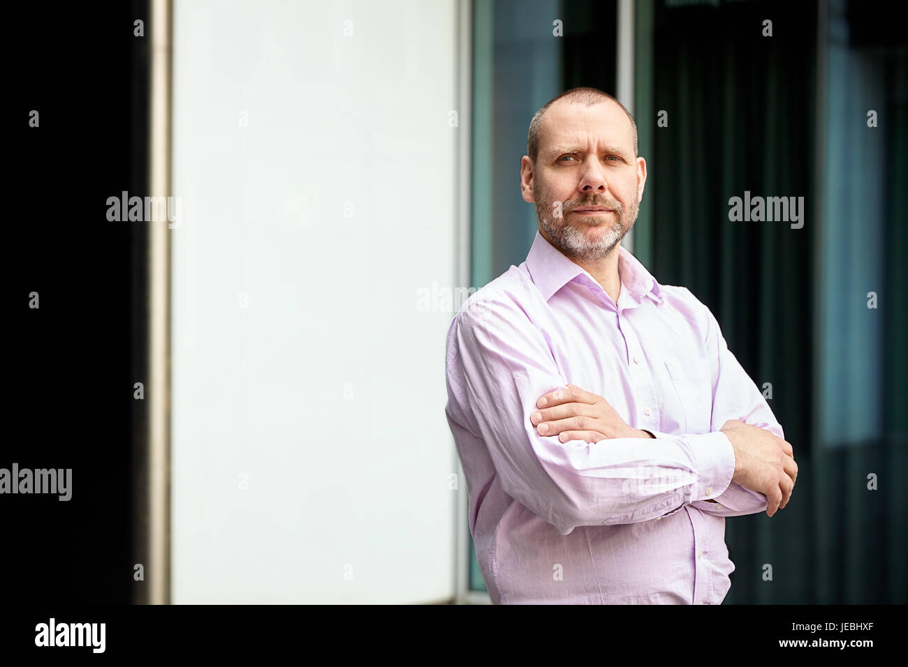Successful businessman standing in front of his office and looking away ...