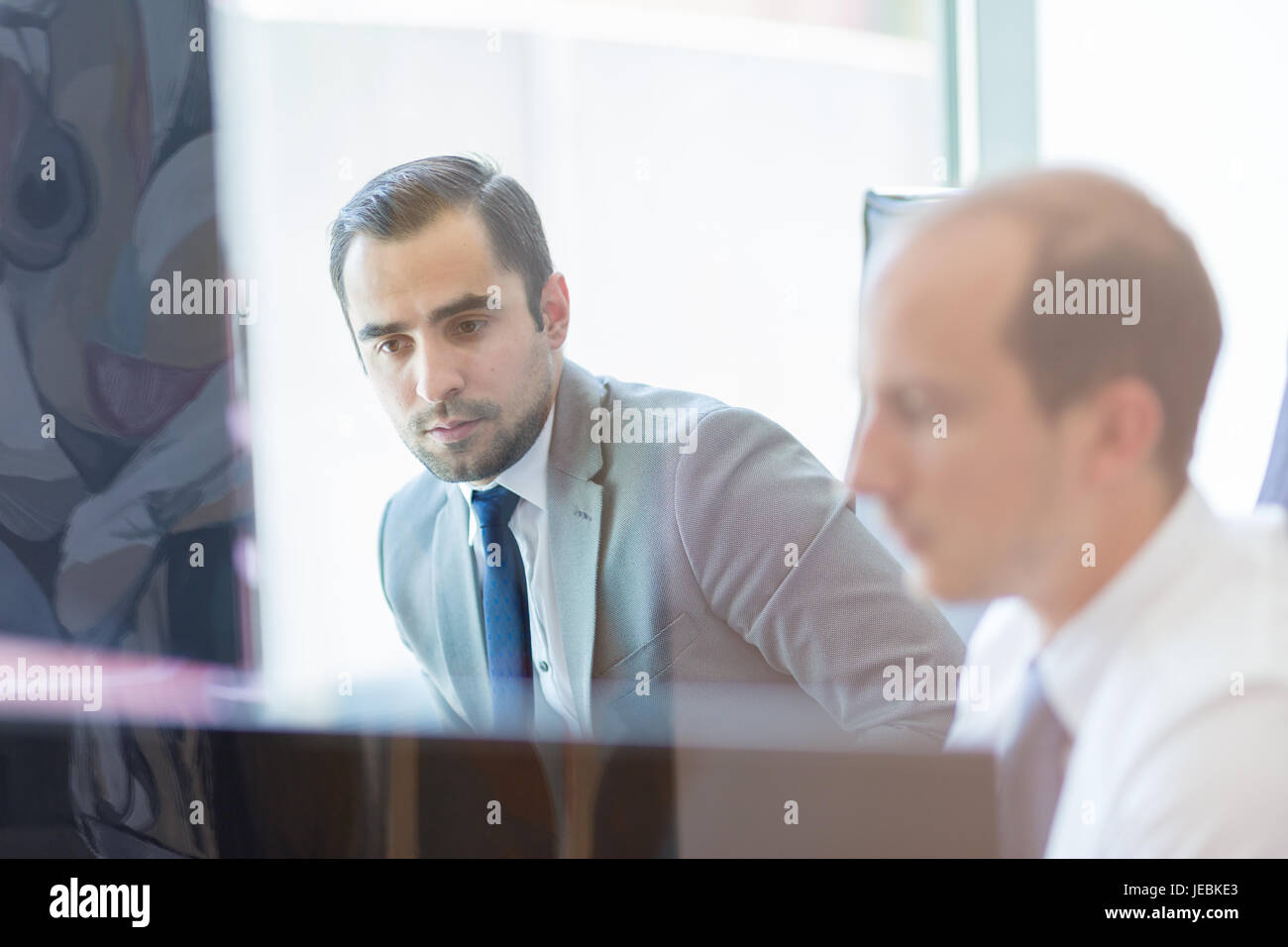 Image of two thoughtful businessmen looking at data on computer screens ...