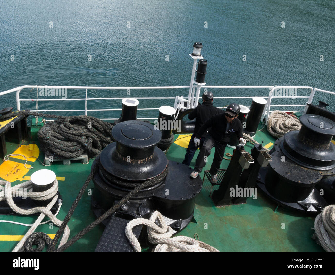 Workers on ship winding in mooring ropes ready to cast off dock lines ...