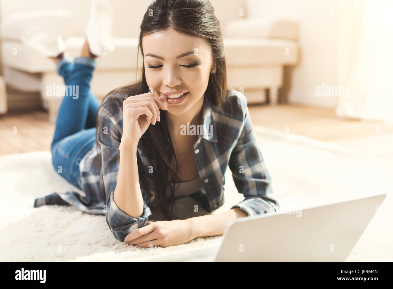 Front view of pretty woman lying on carpet and looking at laptop ...