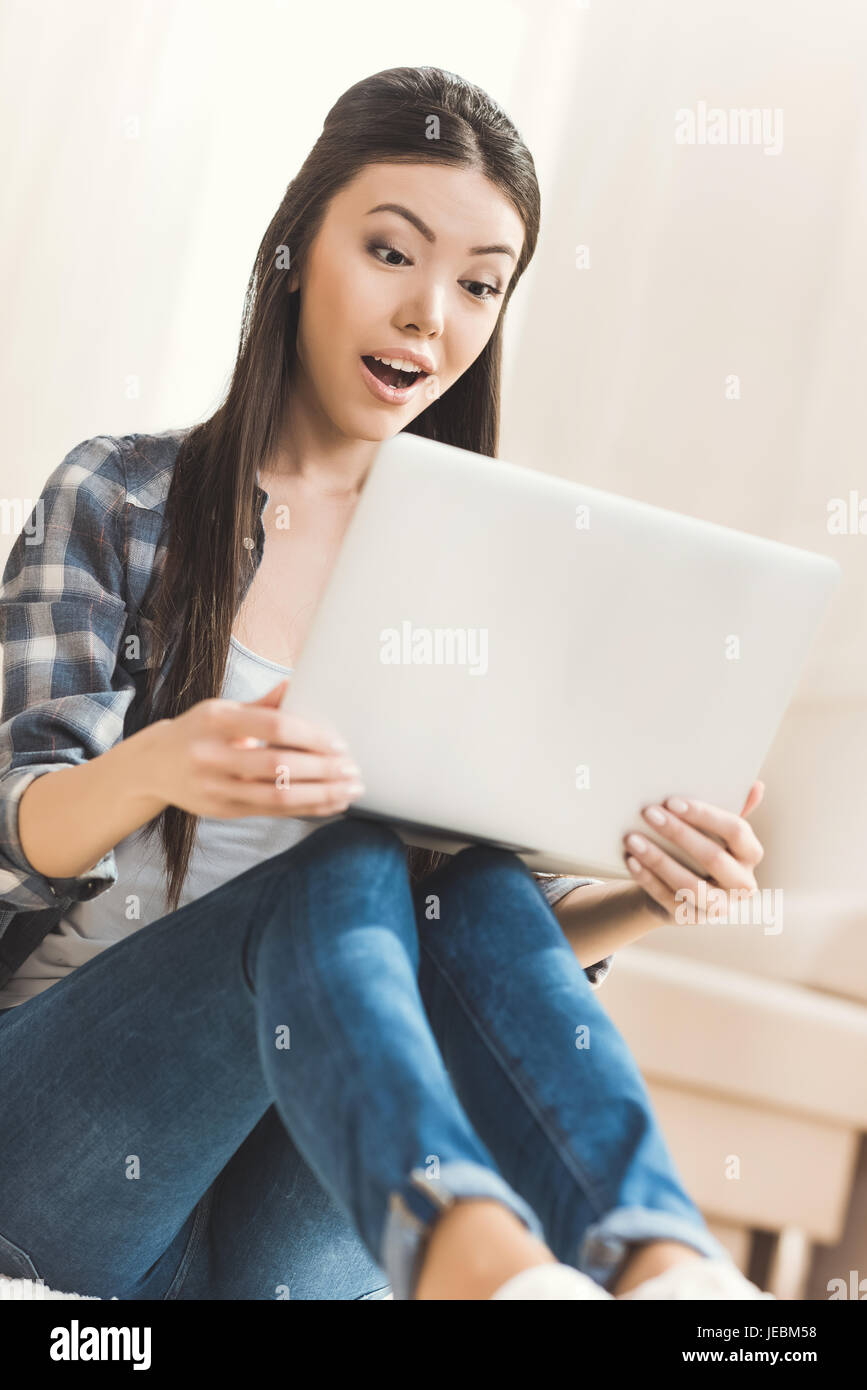 Front view of pretty woman sitting on floor and looking at laptop with ...