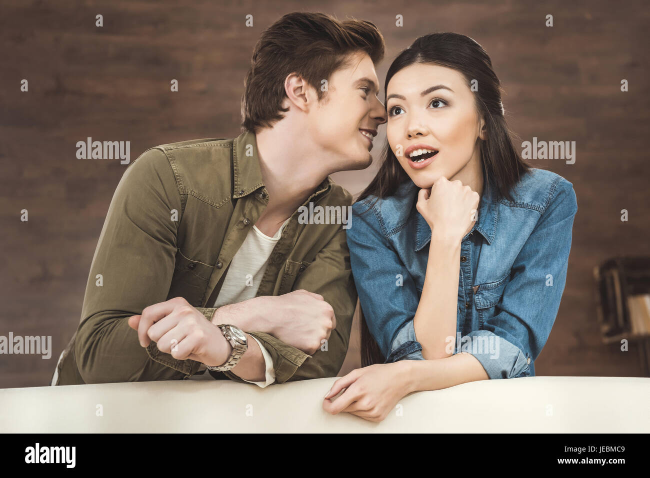 Couple leaning on sofa and man whispering to female ear Stock Photo - Alamy