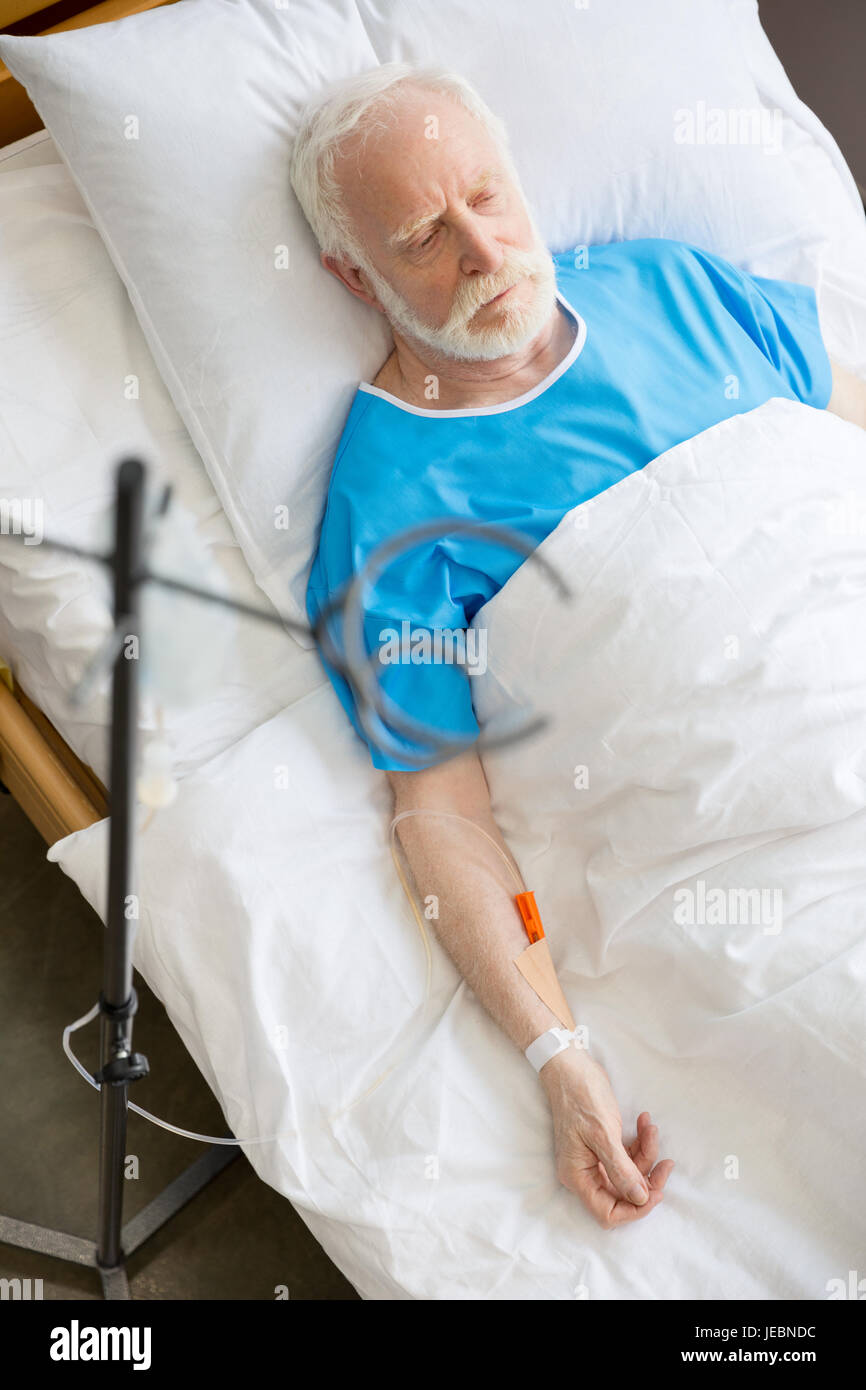 High angle view of bearded senior patient with drop counter lying in ...