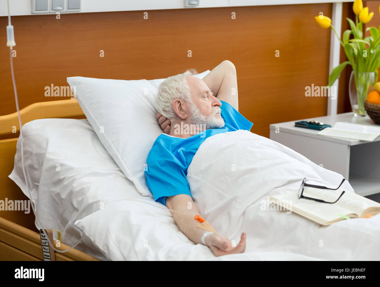 Bearded senior patient with book and eyeglasses sleeping in hospital ...