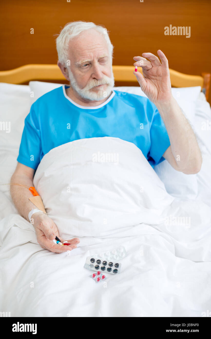 Bearded senior patient in hospital bed holding pills Stock Photo - Alamy