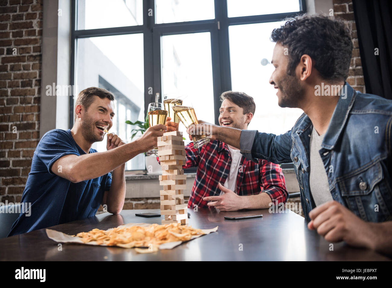 diverse group of young people playing jenga game and drinking beer ...