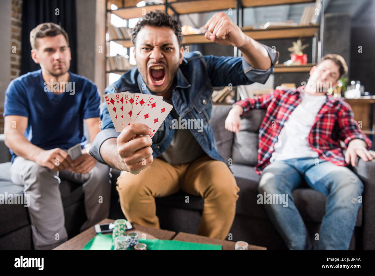 Triumphing young man sitting on sofa and showing street flash of ...
