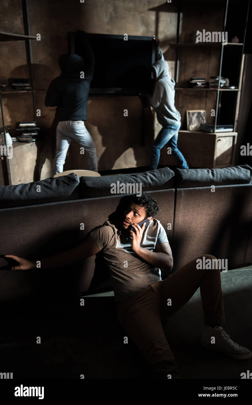 Scared man hiding from robbers behind sofa and calling 911, House ...